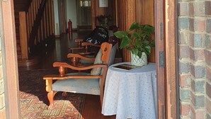 Um arco de madeira dá acesso a um espaço com um banco, uma mesa com uma planta e uma escada ao fundo.