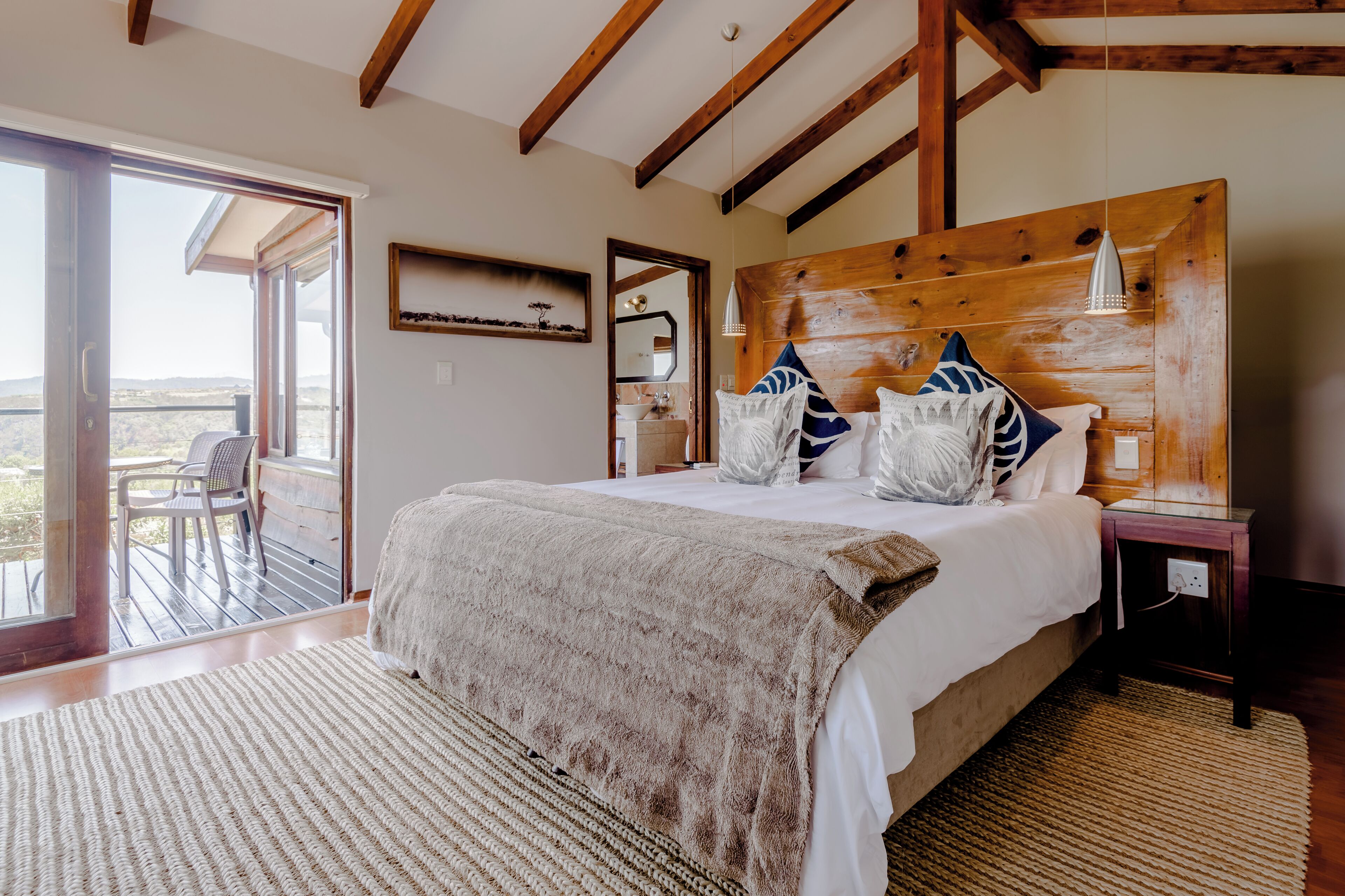 Quarto com cama grande, cabeceira de madeira, mesa de cabeceira, janela e varanda.