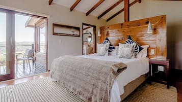 Quarto com cama grande, cabeceira de madeira, mesa de cabeceira, janela e varanda.
