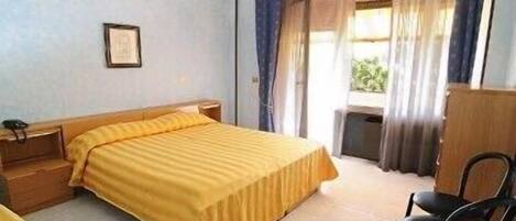 Quarto de hotel com cama, escrivaninha, cadeira e janela com cortinas.