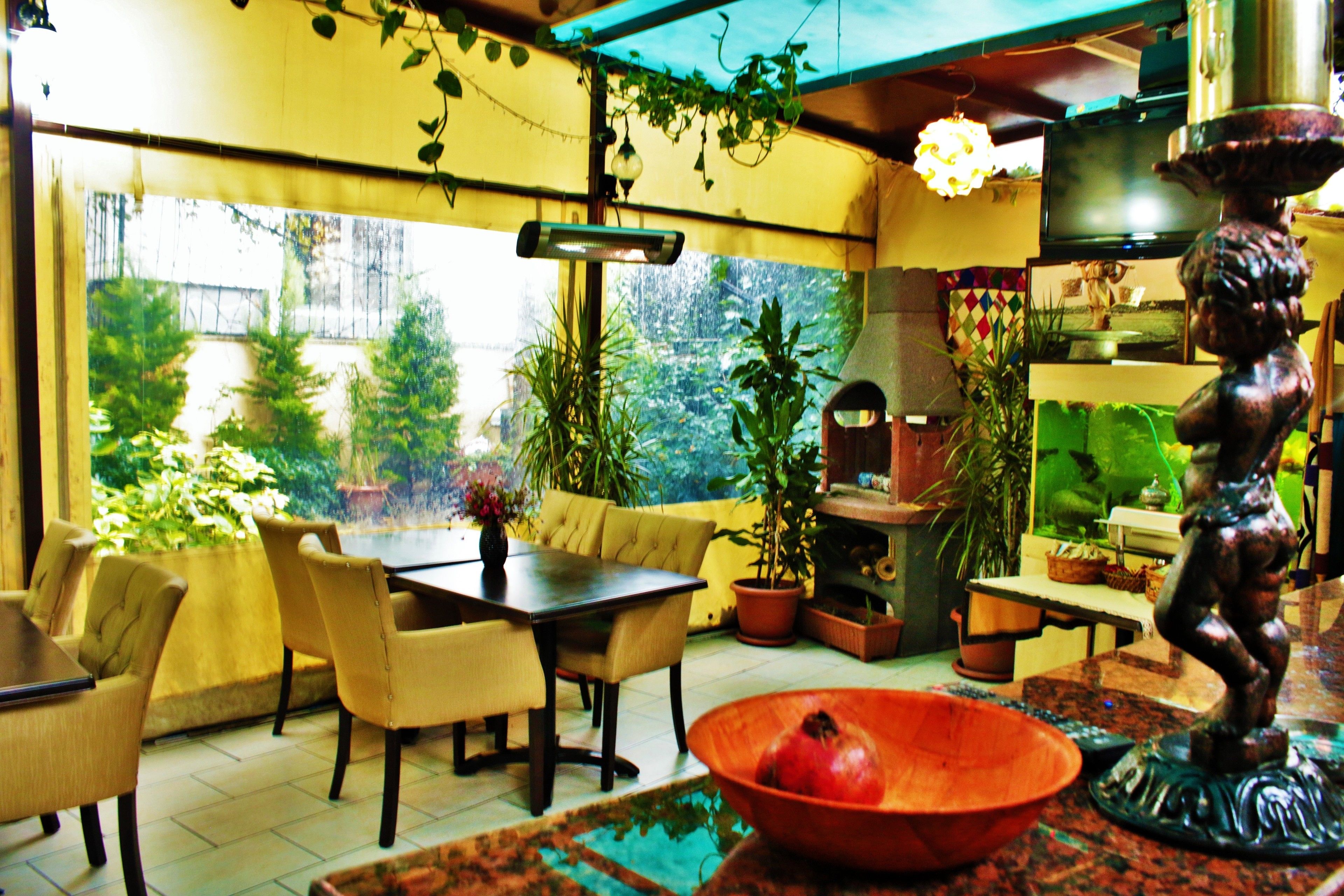 Um espaço interior acolhedor com área de refeições, sofás, uma mesa e plantas em vasos.