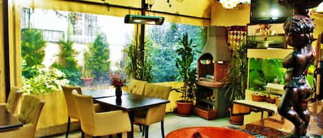 Um espaço interior acolhedor com área de refeições, sofás, uma mesa e plantas em vasos.