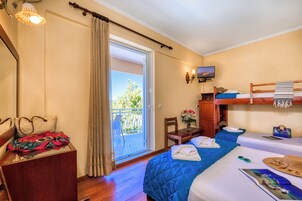 Quarto de hotel com varanda, cama com roupa de cama azul, escrivaninha de madeira e televisão fixada na parede.