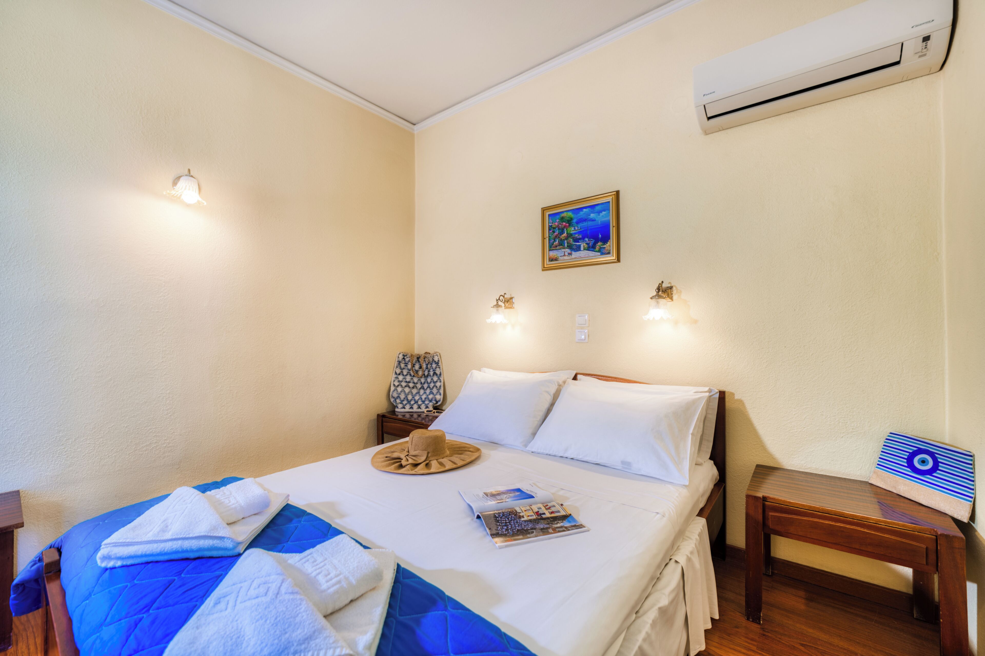 Quarto de hotel com uma cama, mesa de cabeceira, ar condicionado e um quadro na parede.