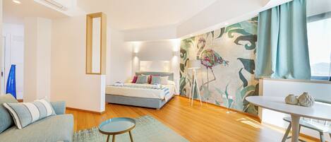 Quarto de hotel moderno com cama, sofá, mesa de jantar e uma janela grande.