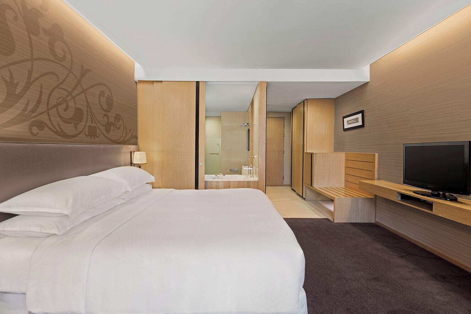 Quarto de hotel moderno com uma cama grande, televisão, banheiro e painel de parede em madeira.