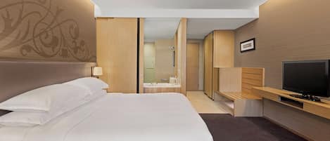 Quarto de hotel moderno com uma cama grande, televisão, banheiro e painel de parede em madeira.