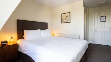 Quarto de hotel com uma cama grande, mesa de cabeceira com abajur, quadro na parede e porta com chave na fechadura.