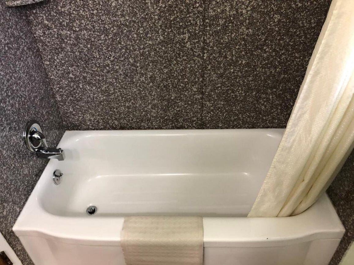 Uma banheira branca com cortina de chuveiro em um banheiro com piso texturizado.