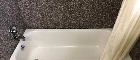 Uma banheira branca com cortina de chuveiro em um banheiro com piso texturizado.
