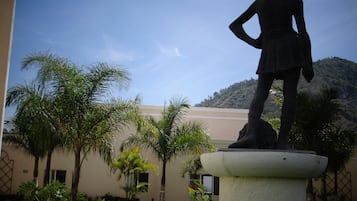 Uma estátua em um pedestal em um pátio com palmeiras e um edifício ao fundo.