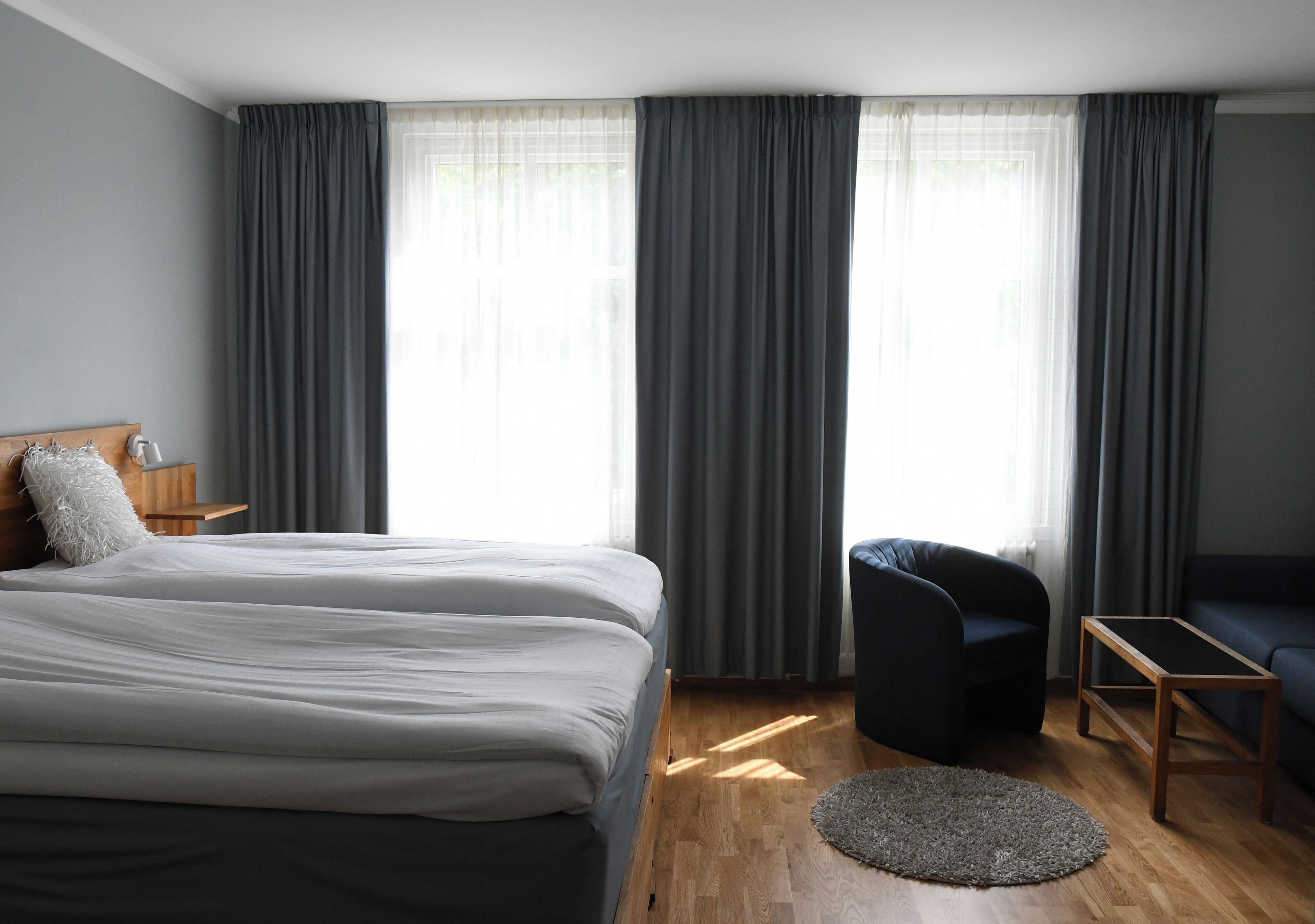 Quarto moderno com uma cama grande, uma mesa de cabeceira de madeira, uma cadeira, uma mesinha e um tapete redondo.