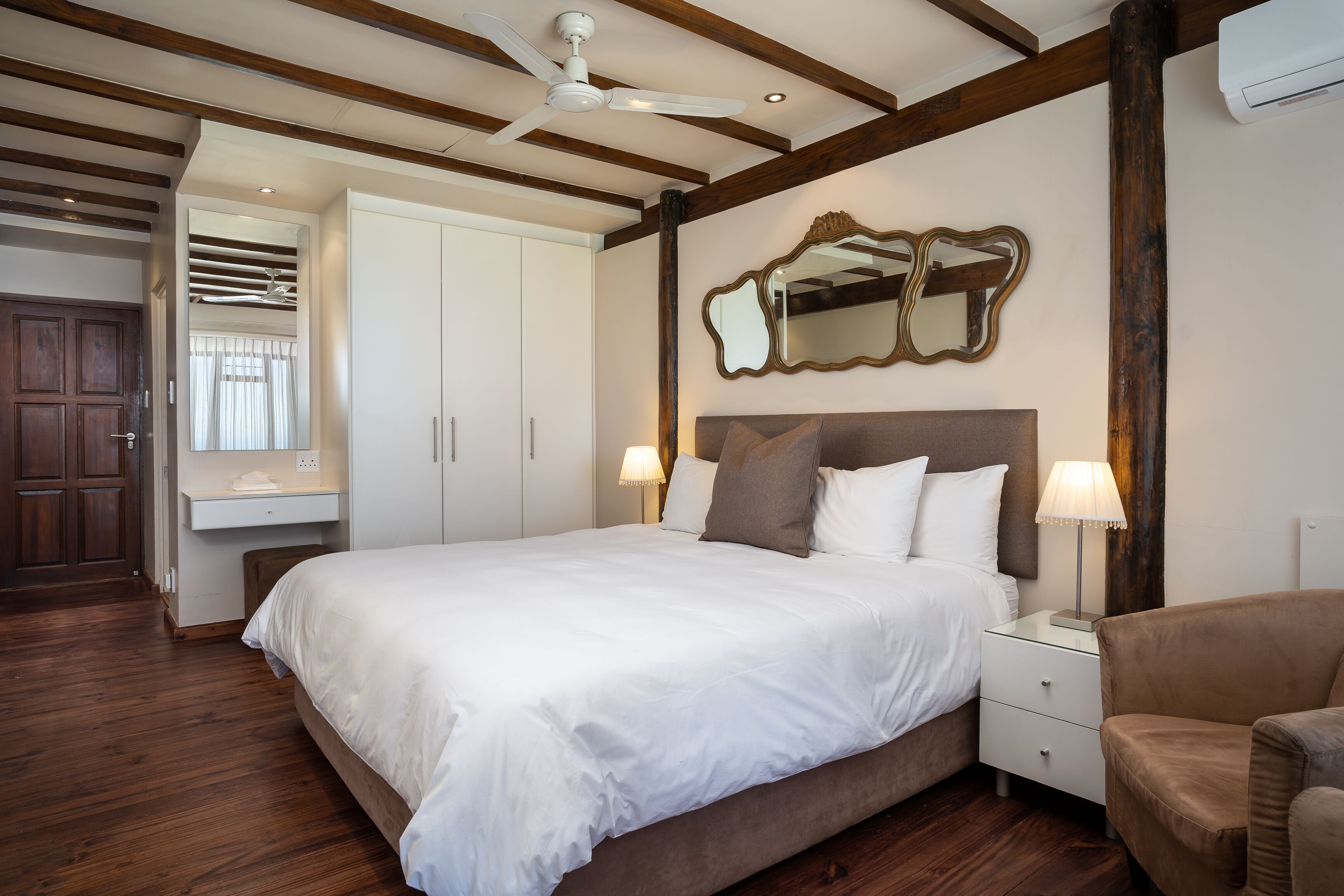 Quarto com uma cama grande, luminárias de cabeceira, ventoinha no teto e teto de madeira.