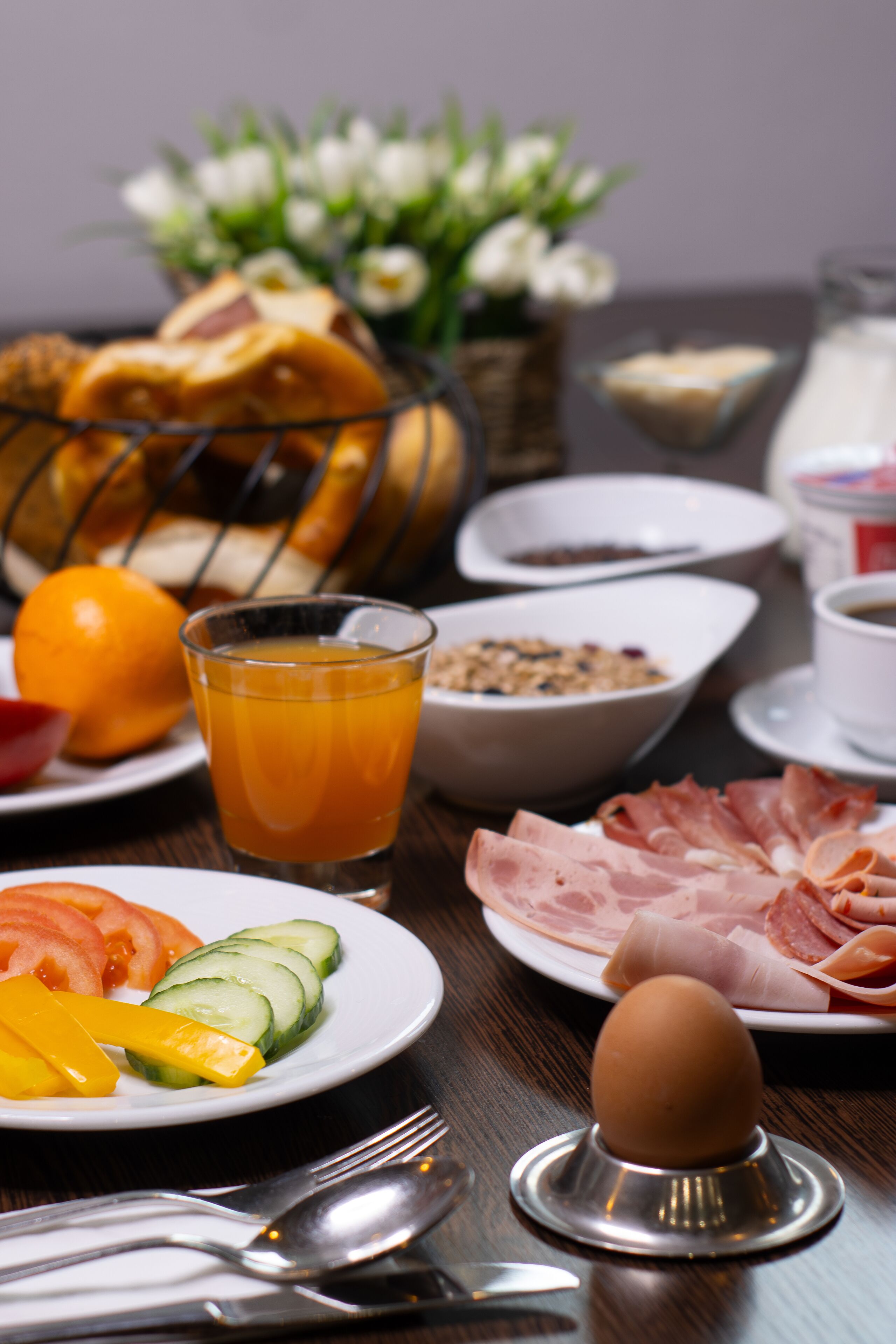 Uma mesa de café da manhã com pratos de comida, um copo de suco de laranja e uma cesta de pão.
