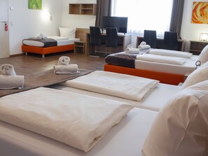 Quarto de hotel com várias camas, uma escrivaninha e uma televisão.