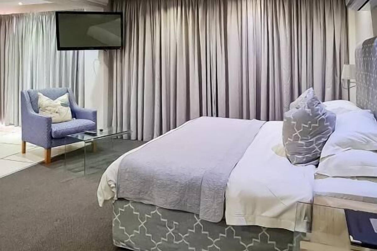 Quarto moderno com cama grande, uma cadeira, televisão e cortinas.