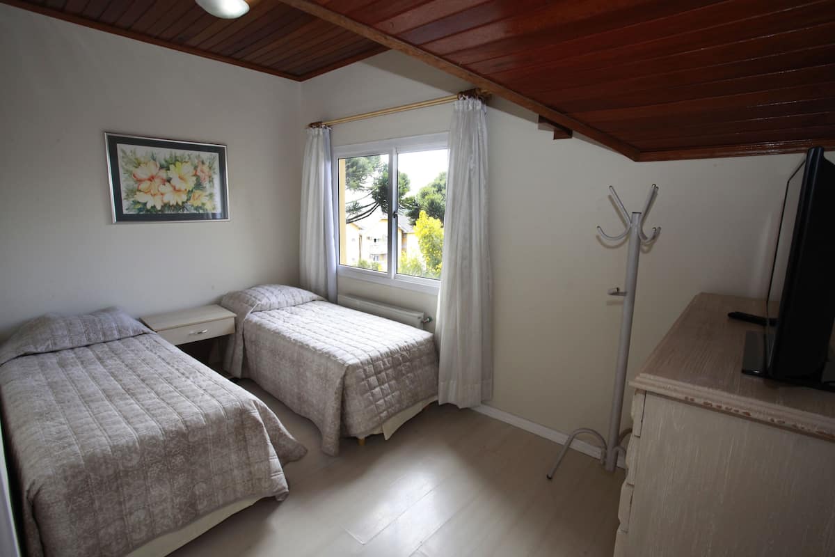Quarto com duas camas, uma janela com cortinas, um porta-roupas e um quadro na parede.