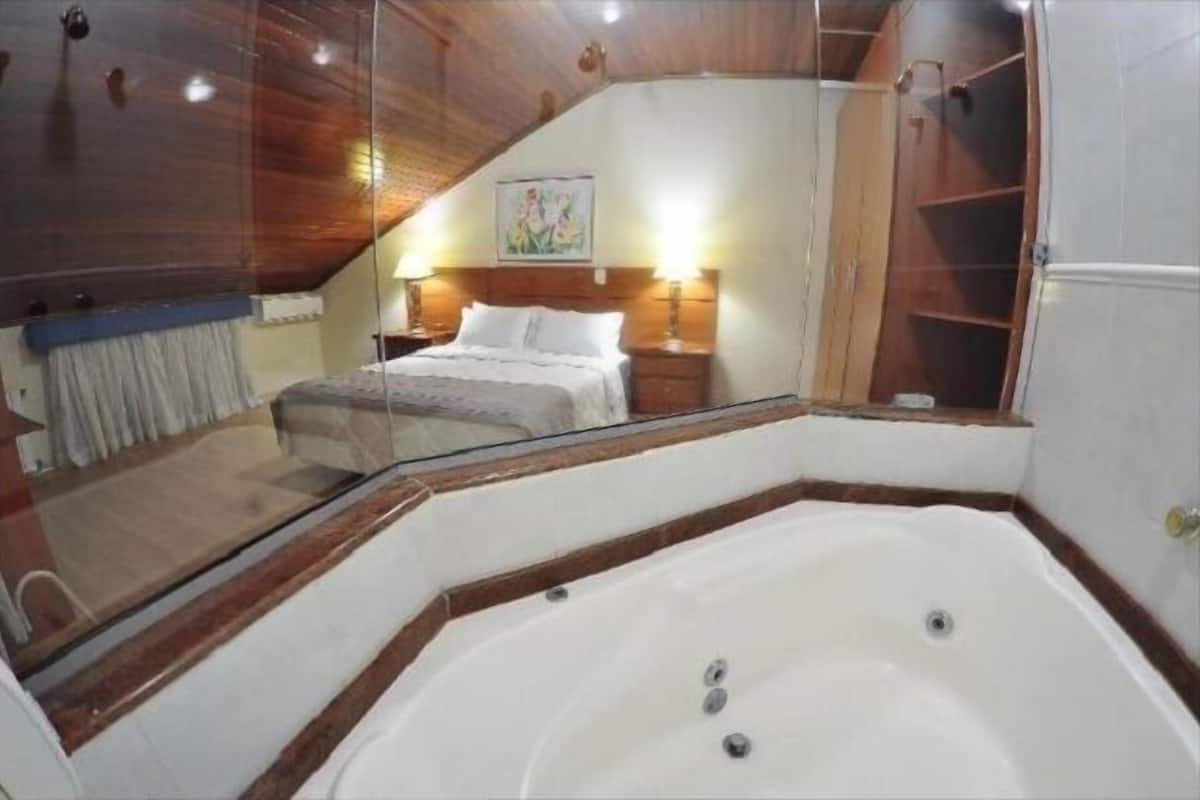 Quarto com cama grande, teto de madeira, banheira branca e guarda-roupa de madeira.