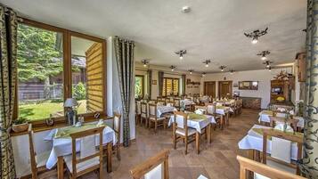 Uma sala de jantar com várias mesas e cadeiras, janelas amplas e vista para o exterior.