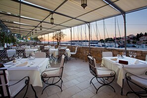 Restaurante ao ar livre com mesas preparadas para refeições, com vista para uma marina e barcos.