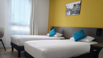 Quarto de hotel com duas camas, piso de madeira, janela com cortinas e um quadro pendurado na parede.