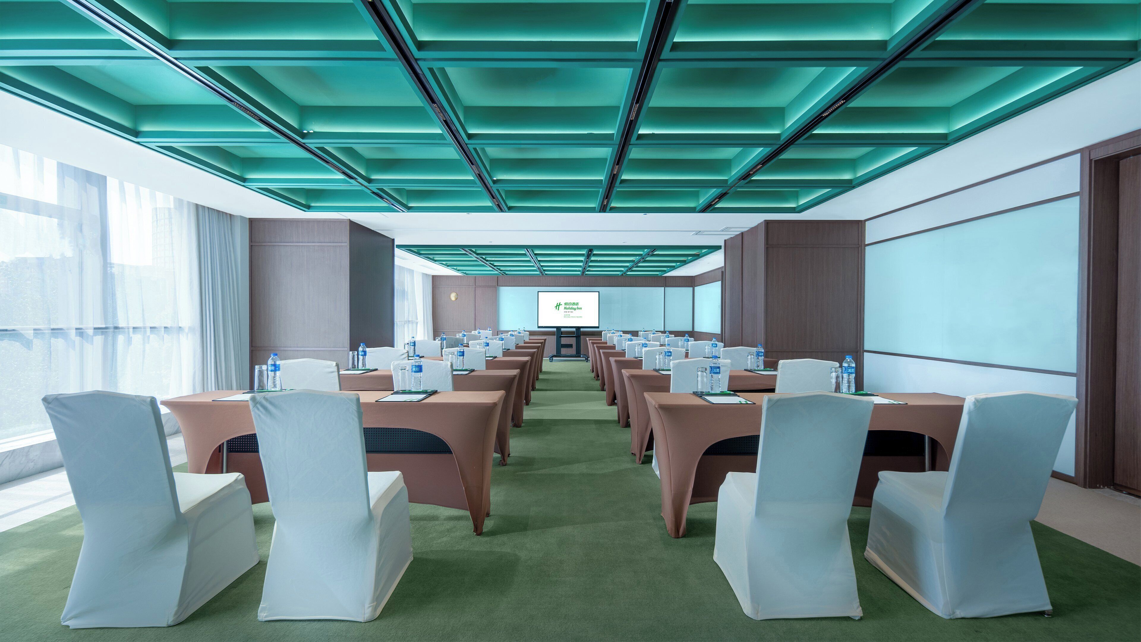 Sala de conferências com carpete verde, cadeiras brancas e mesas organizadas para uma reunião.