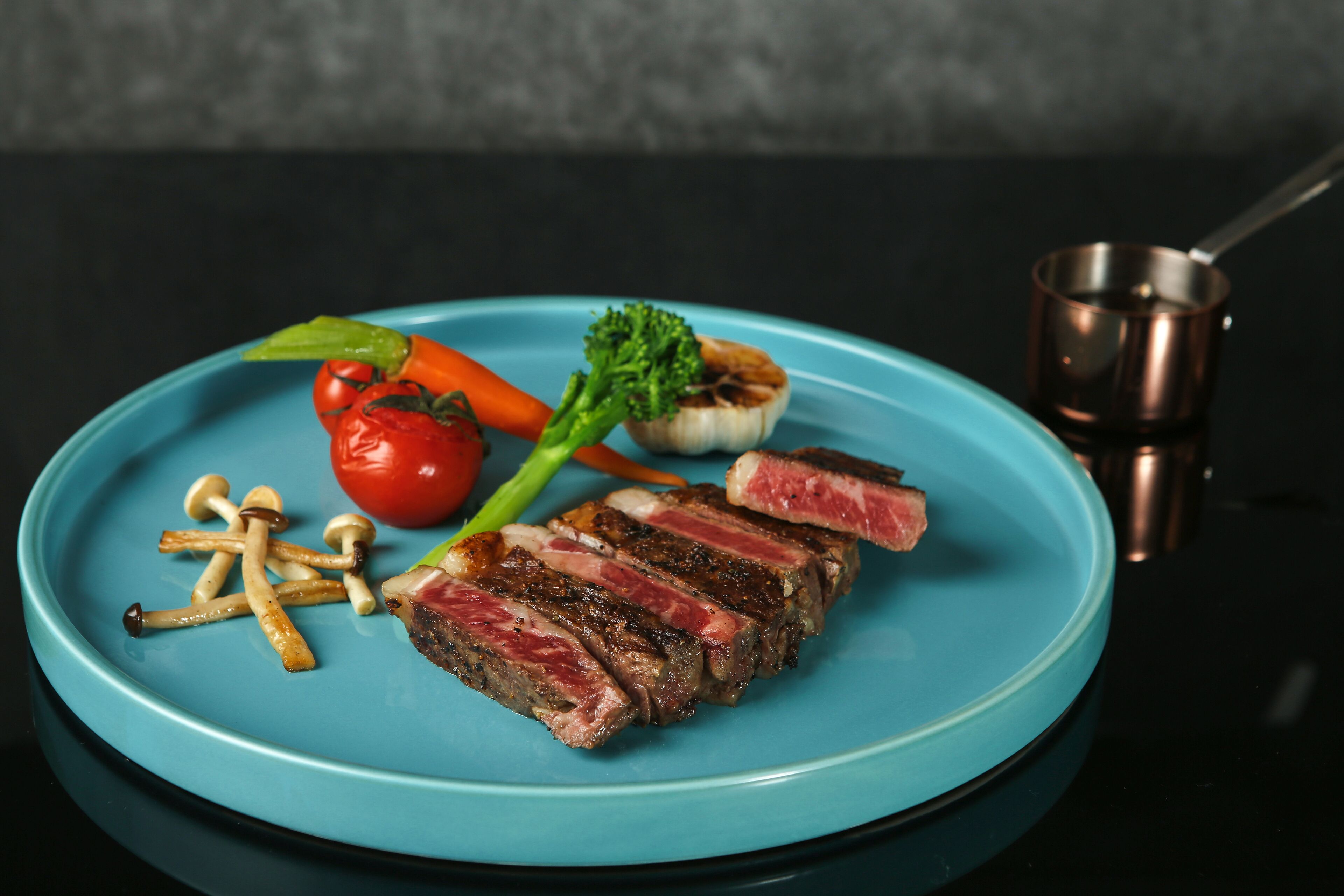 Um prato azul com bife fatiado, cogumelos, tomate e brócolis.