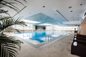 Piscina interna com água cristalina, rodeada por um chão de azulejos e um teto com padrão geométrico.
