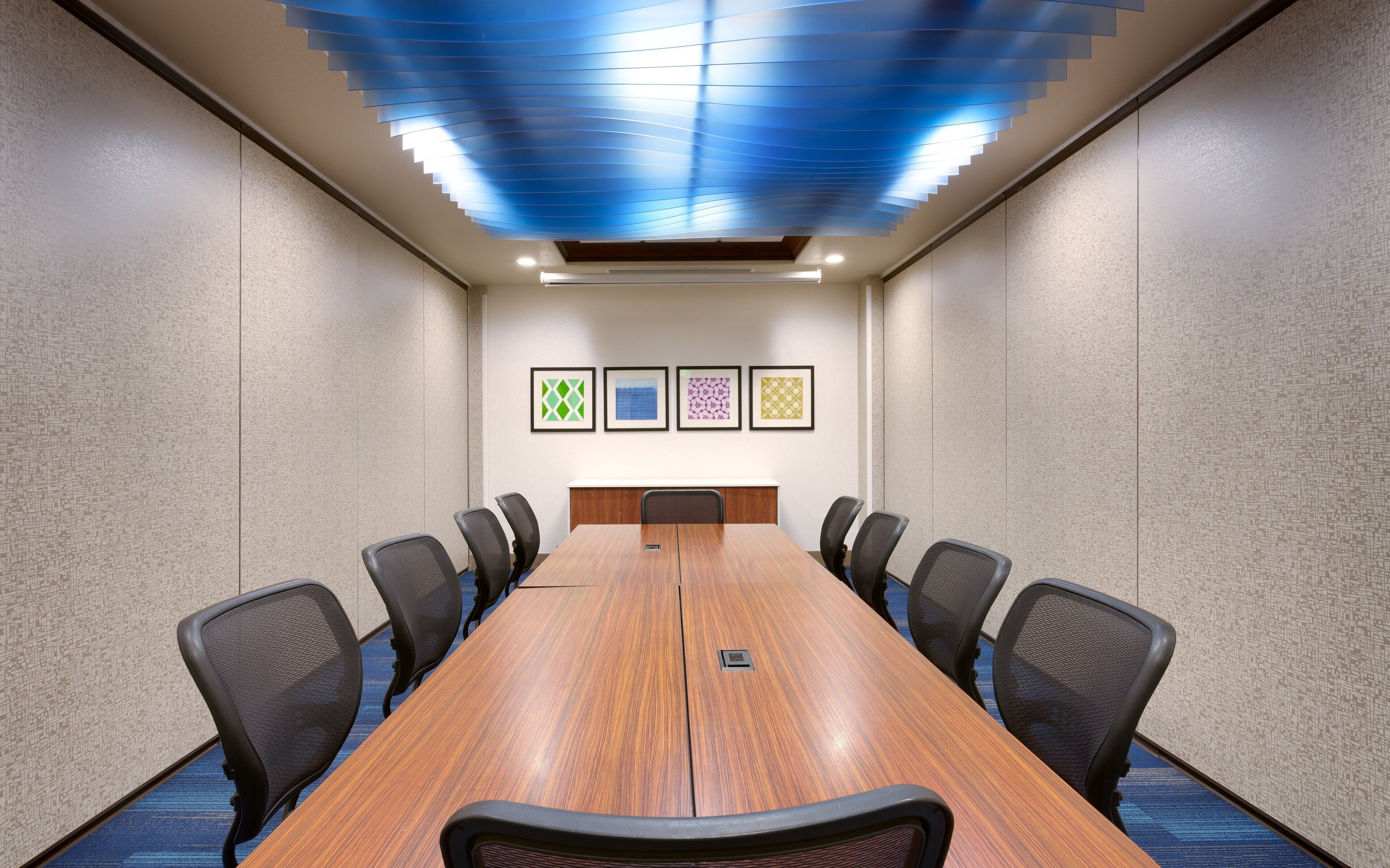 Uma sala de conferências com uma longa mesa de madeira, seis cadeiras e teto decorado.