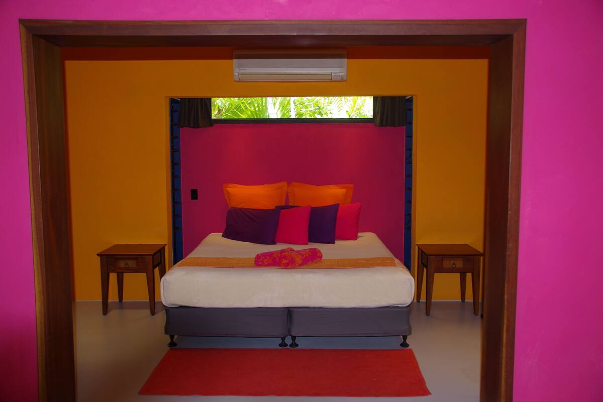 Quarto com uma cama, duas mesas de cabeceira, uma janela e um tapete vermelho.