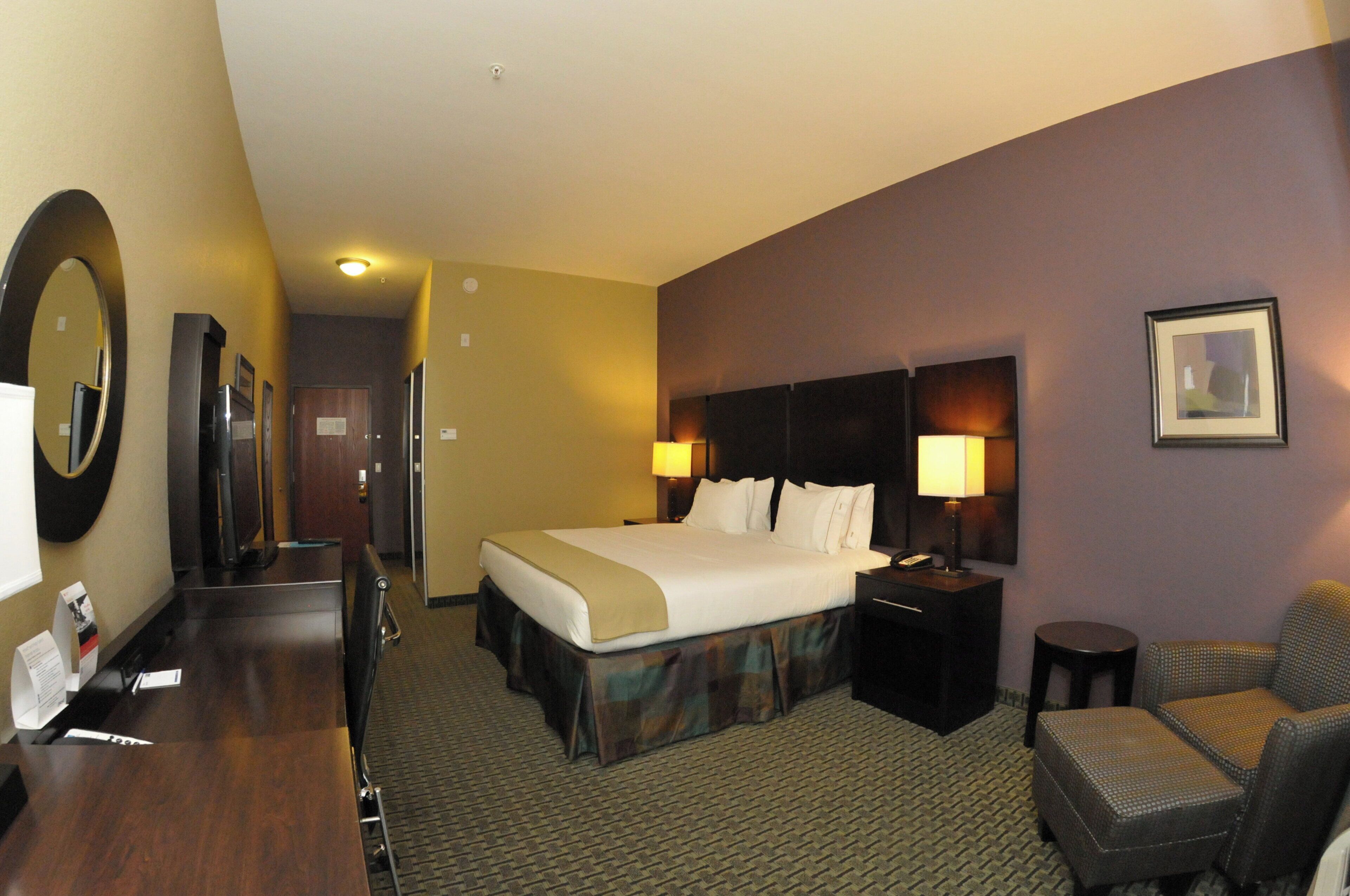 Quarto de hotel com cama, mesas de cabeceira, uma cadeira, escrivaninha e espelho.
