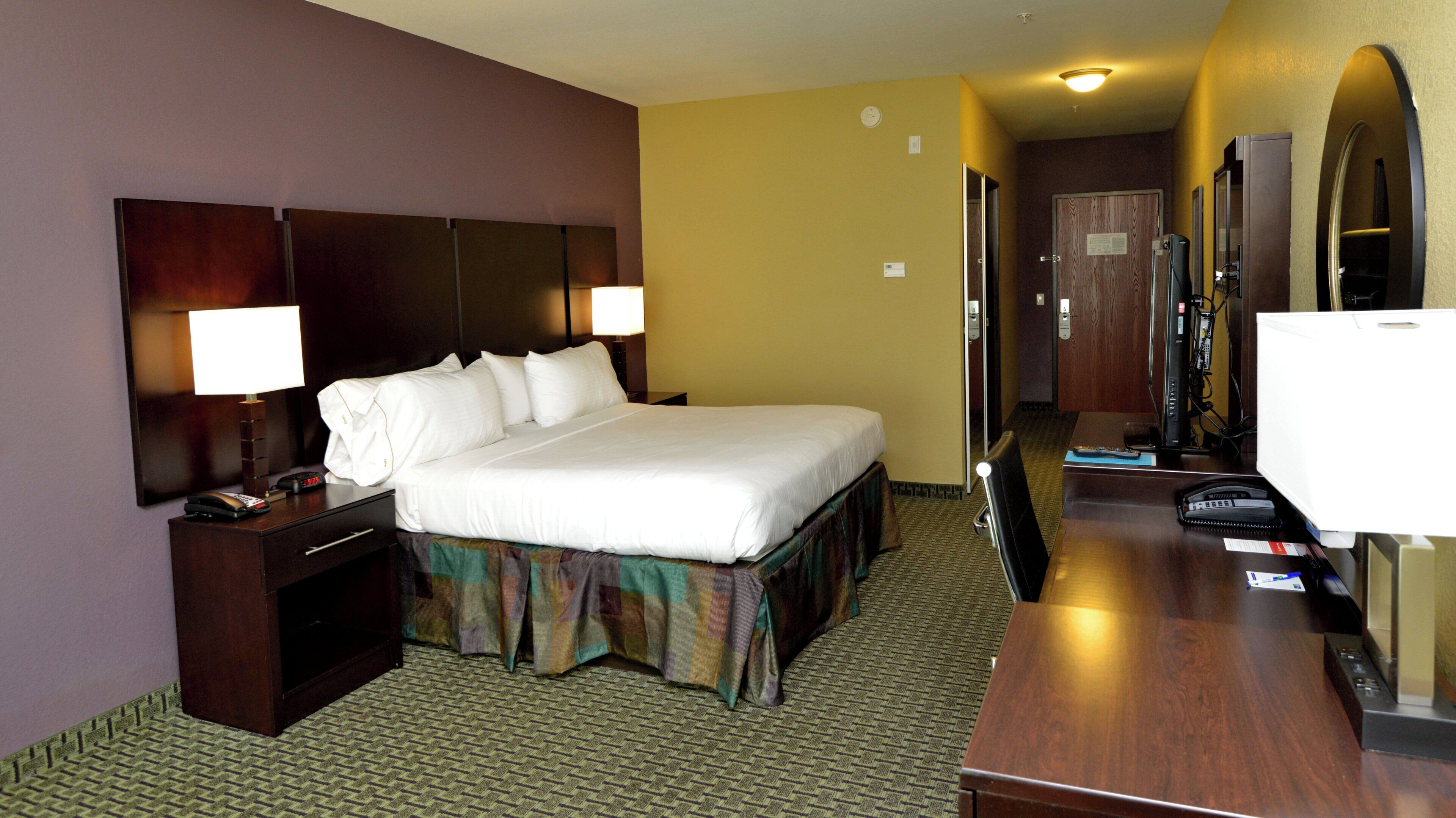 Quarto de hotel com cama, mesas de cabeceira, escrivaninha e espelho.