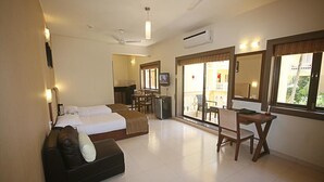 Quarto de hotel com duas camas, uma escrivaninha, uma cadeira, uma televisão e uma varanda com vista.