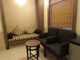 Um quarto pequeno e acolhedor, com um sofá, uma poltrona, uma mesa redonda e uma janela com persianas.