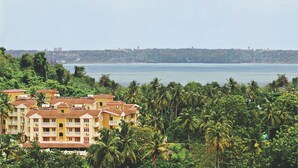 Um hotel à beira-mar, com vários andares, rodeado por vegetação exuberante e vista para o mar.
