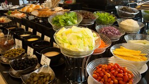 Buffet com diversos alimentos, incluindo azeitonas, salada e milho.