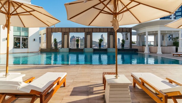 Uma área de piscina no terraço com espreguiçadeiras e guarda-sóis, cercada por edifícios modernos e um horizonte urbano.