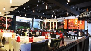 Restaurante com várias mesas preparadas para refeições, com guardanapos vermelhos e toalhas de mesa brancas.