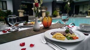 Mesa de jantar posta para dois, com pratos de comida, copos de água e um vaso com flores.