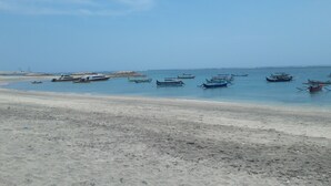 Uma praia com barcos ancorados na água e um molhe rochoso ao fundo.