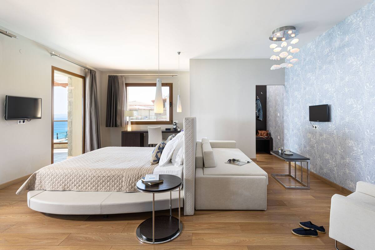 Quarto de hotel moderno com uma cama grande, um sofá, uma pequena mesa e uma televisão.