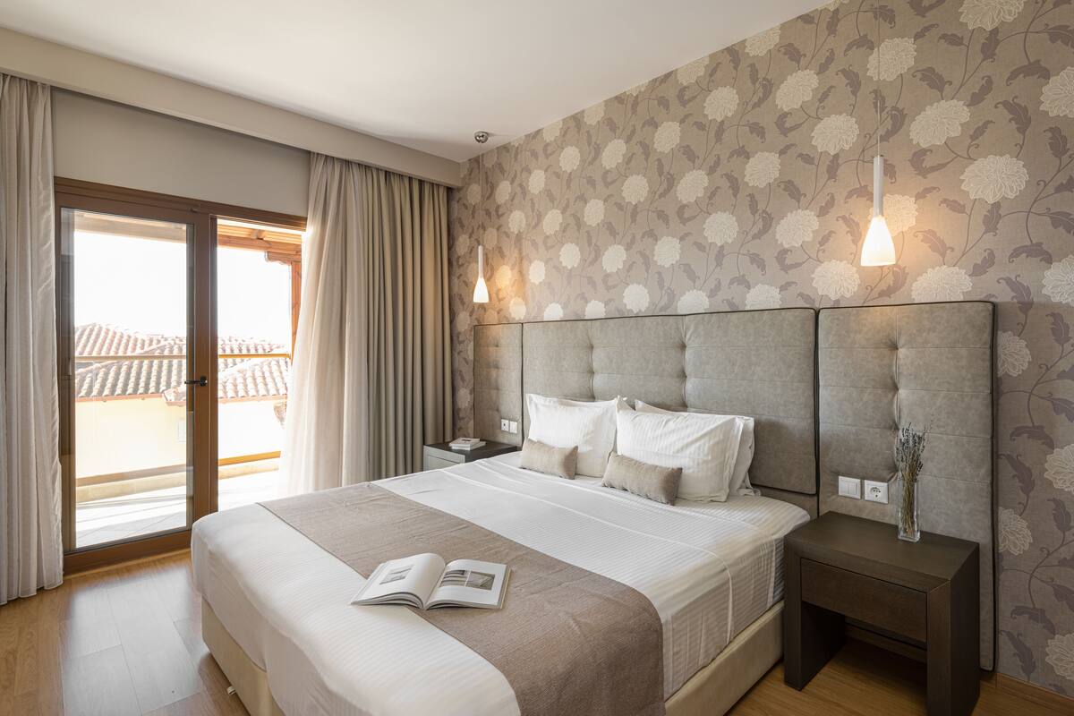 Quarto de hotel com uma cama grande, mesa de cabeceira, luminária e vista para o exterior.