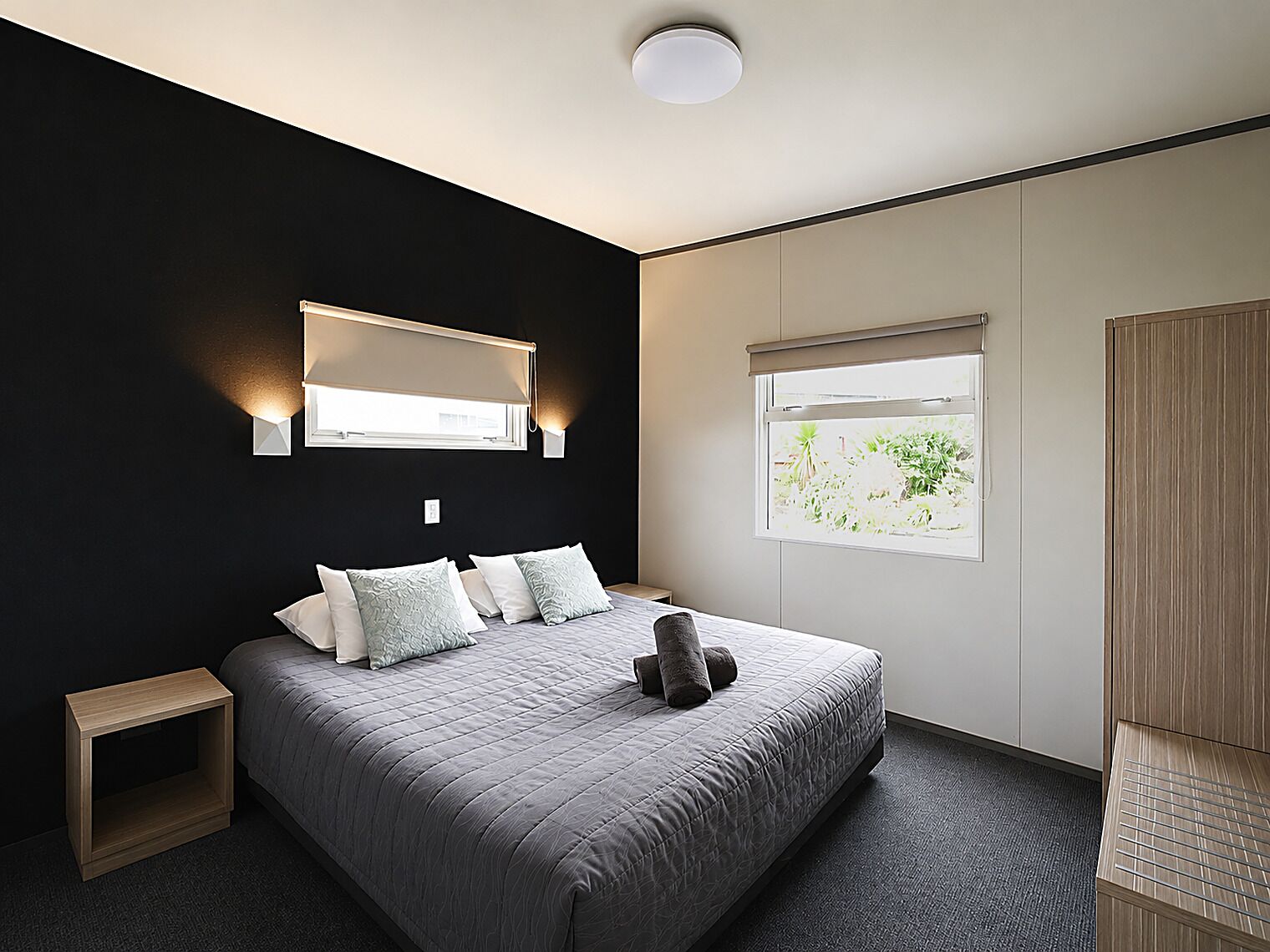 Quarto moderno com cama grande, mesas de cabeceira, janela com persianas e luminária no teto.