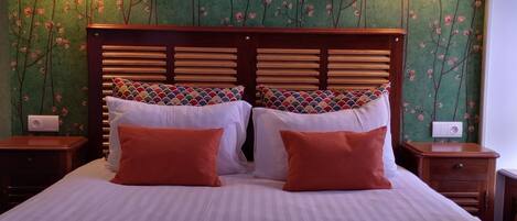 Cama bem arrumada com roupa de cama listrada, duas almofadas vermelhas e cabeceira de madeira.