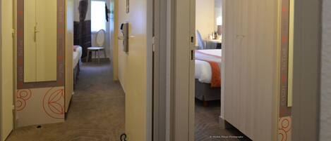 Corredor de hotel com uma cama, uma cadeira e uma escrivaninha.