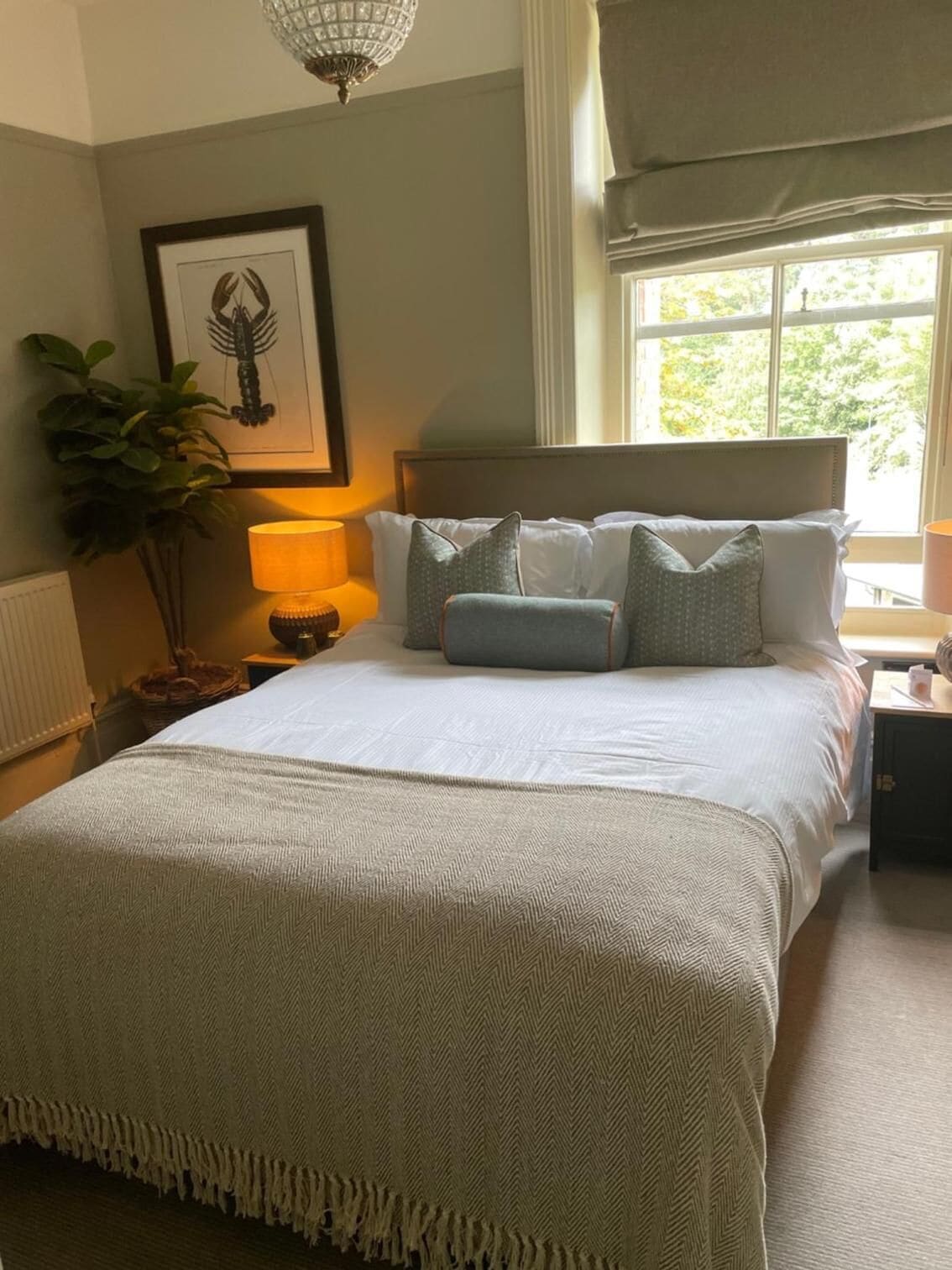 Cama bem arrumada com colcha de padrão matelassê, cabeceira e várias almofadas.