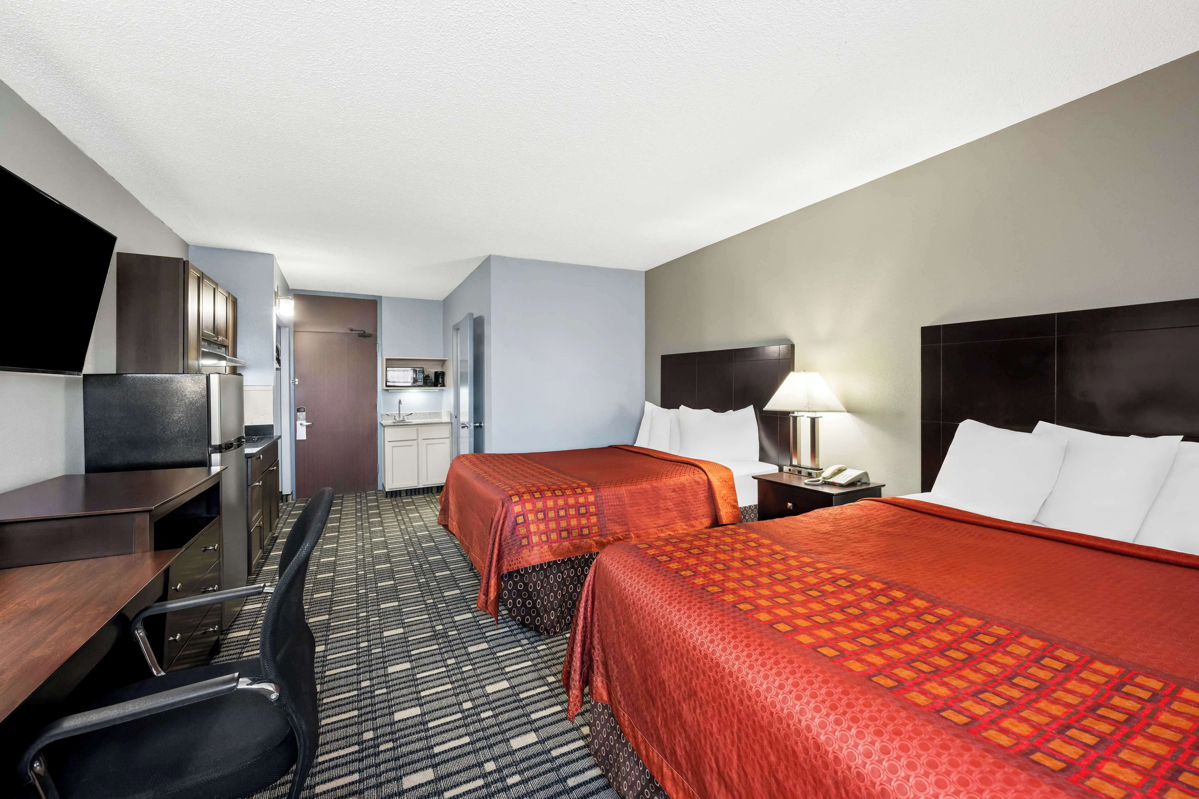 Quarto de hotel com duas camas, uma escrivaninha, uma cadeira, luminária de mesa e mesa de cabeceira com telefone.