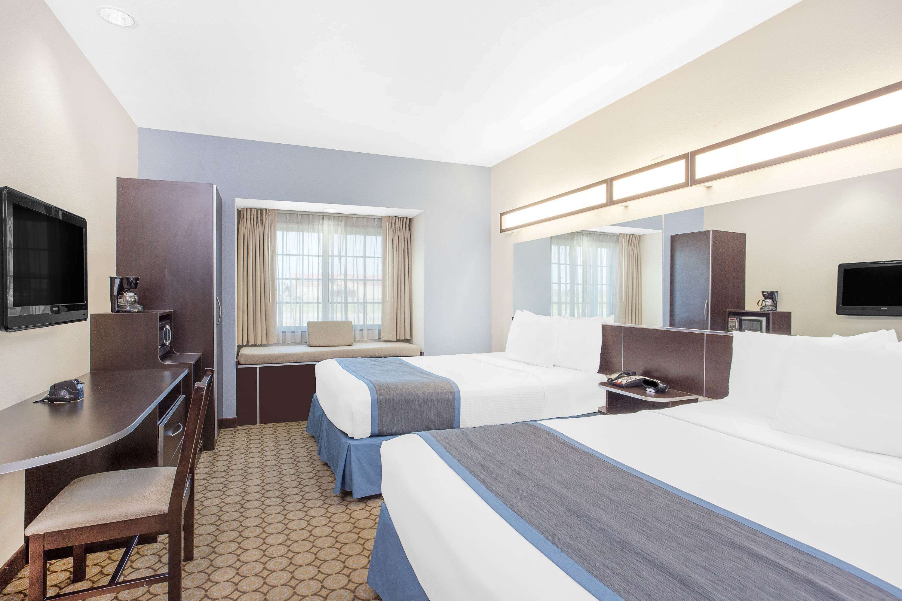 Quarto de hotel com duas camas, uma escrivaninha, uma cadeira, uma televisão e um espelho grande.