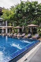 Piscina com espreguiçadeiras e guarda-sóis, cercada por vegetação.
