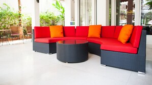 Uma área de estar moderna ao ar livre, com um sofá vermelho e almofadas laranja, uma mesa redonda e mobiliário de vime.